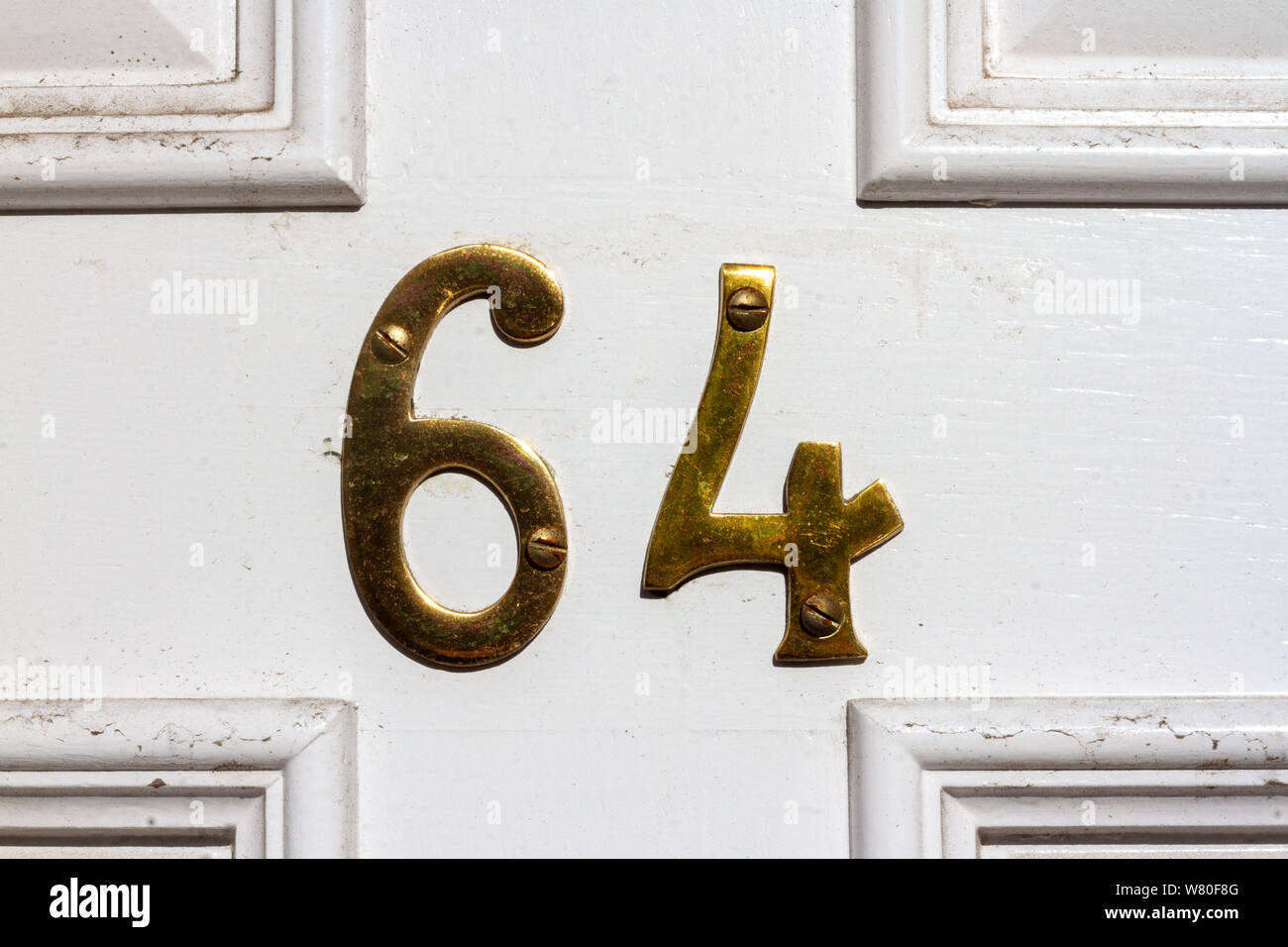 House number 64 in bronze metal digits on a white wooden front door ...