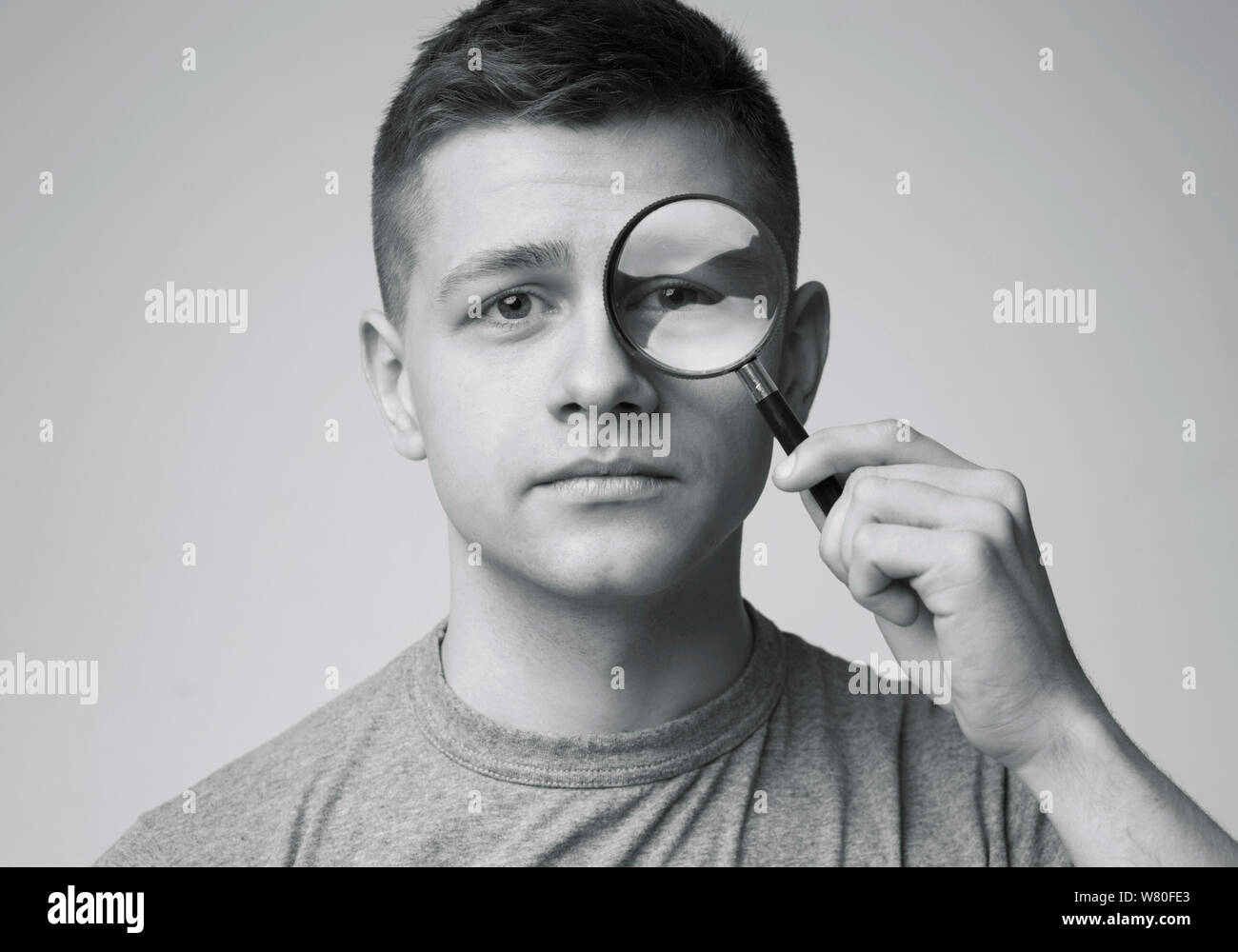 Portrait of young man looking through magnifying glass Stock Photo - Alamy