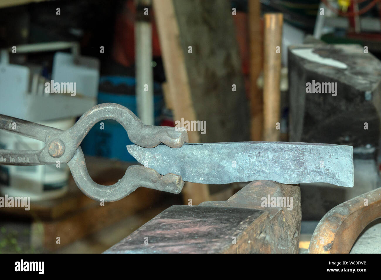 The professional knife maker holds a work in progress with tongs on the ...