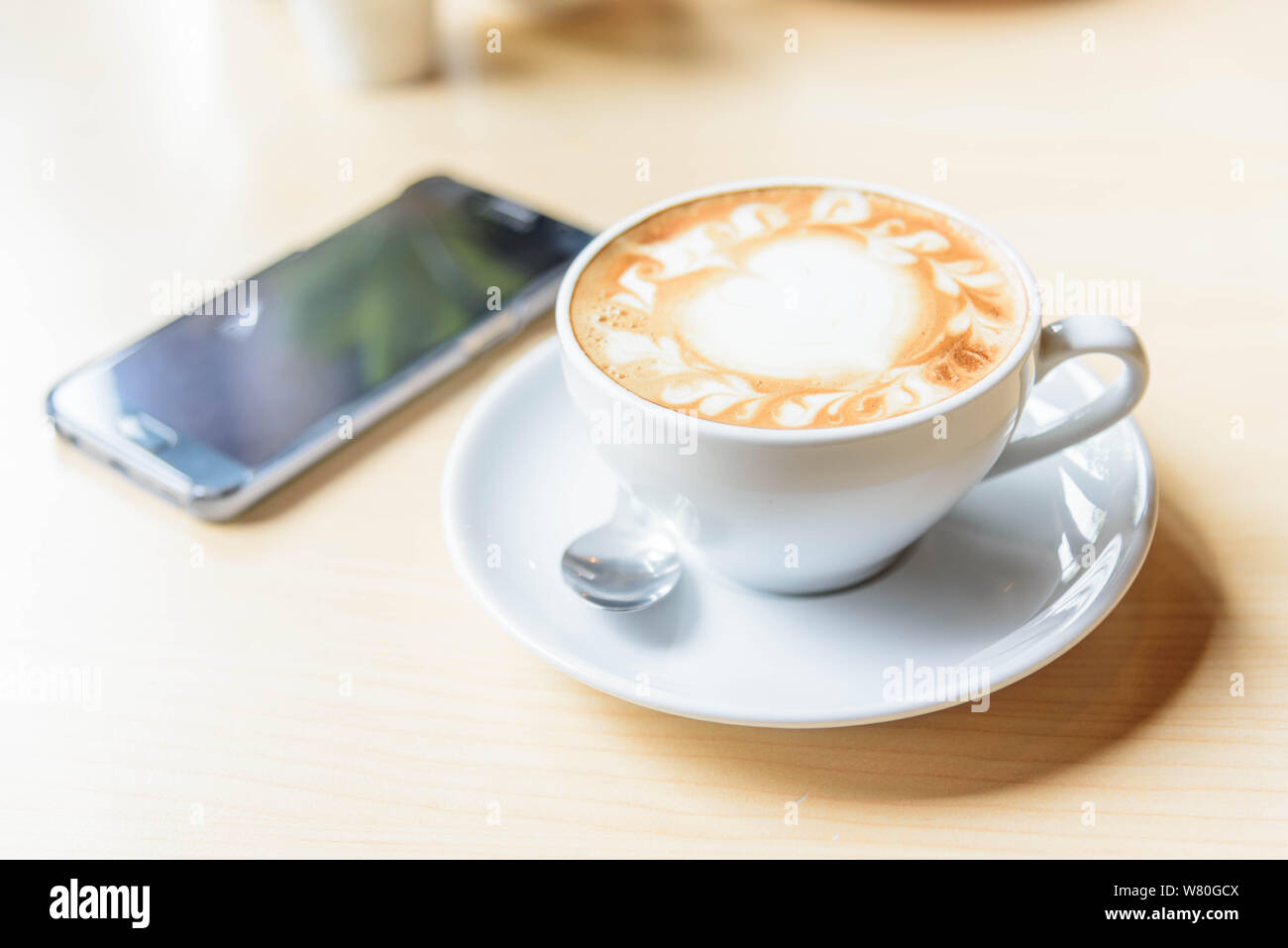 hot cappuccino with nice milk pattern and smart phone on work space ...