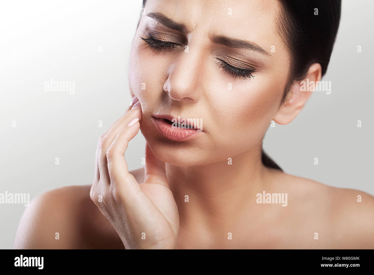Beautiful young woman suffering from a toothache on a gray background ...