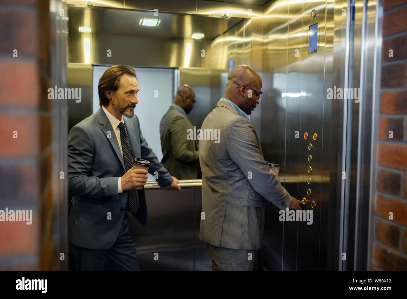 Man pressing button in elevator while standing near colleague Stock ...