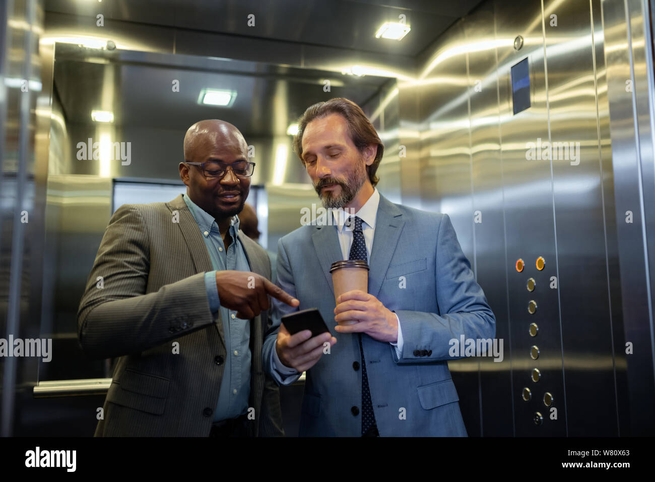 Two businessmen reading info on smartphone while using elevator Stock ...