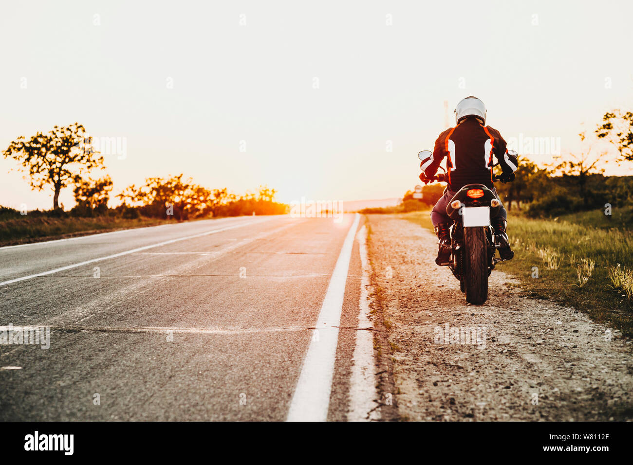Back view of a equiped biker sitting on his motorcycle stopping on the ...