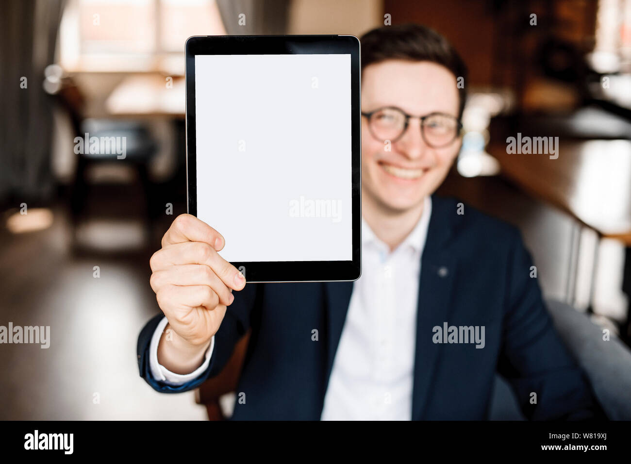 Adult man dressed in suit holding a tablet in front of his face showing ...