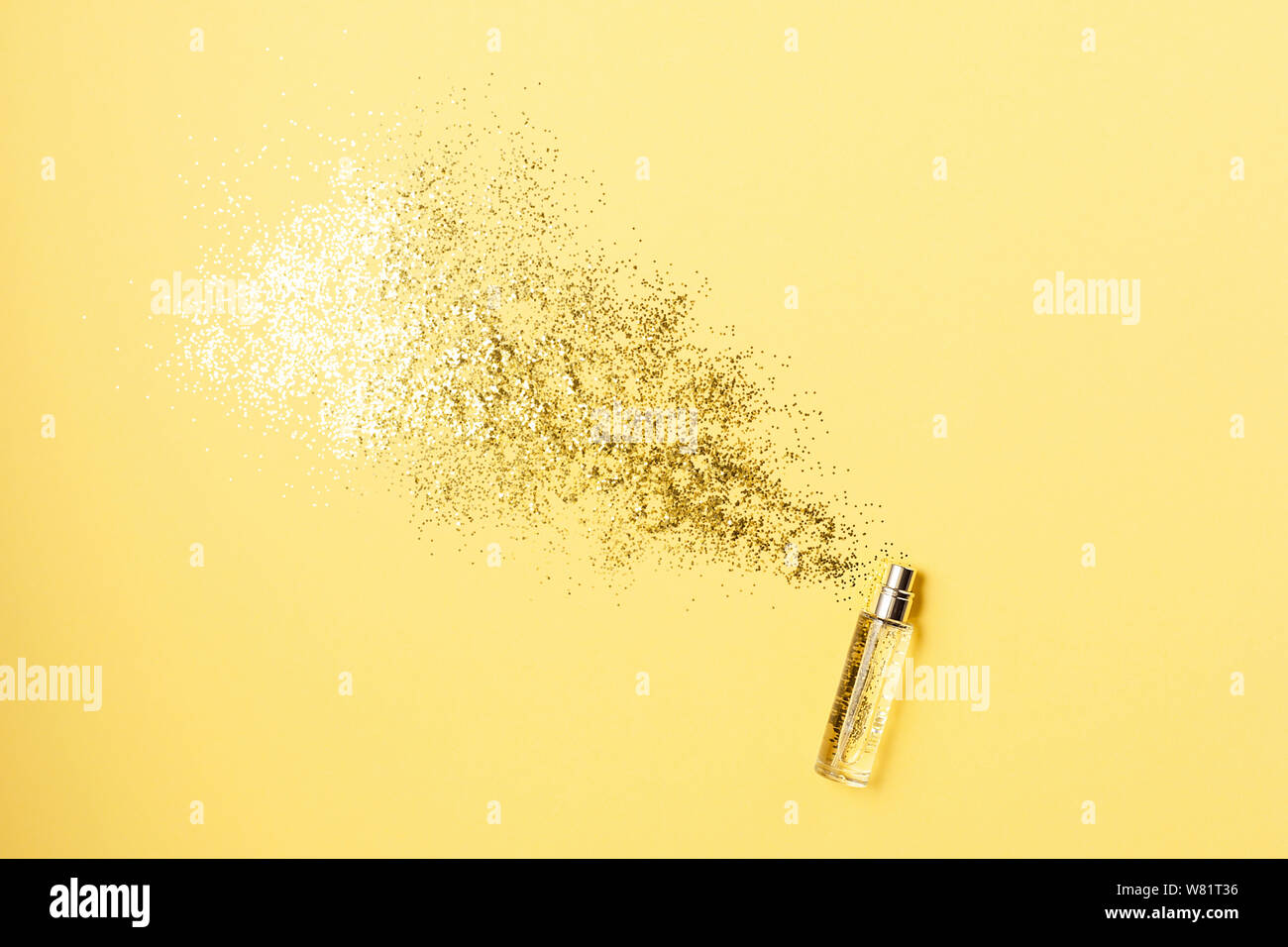 Stylish bottle of perfume with spray of sparkles on yellow background ...