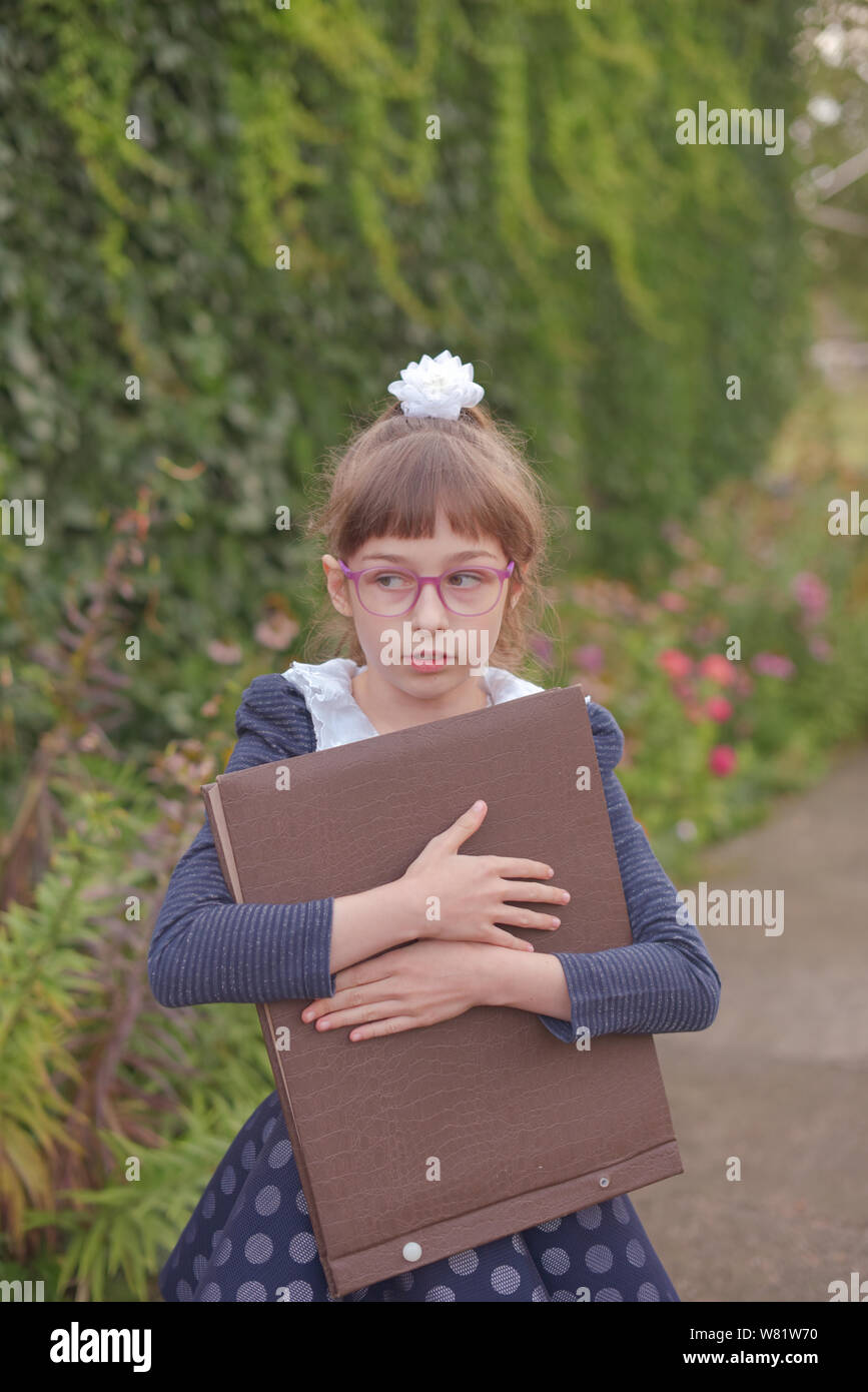 Schoolgirl with a big brown notebook on a background of greenery ...
