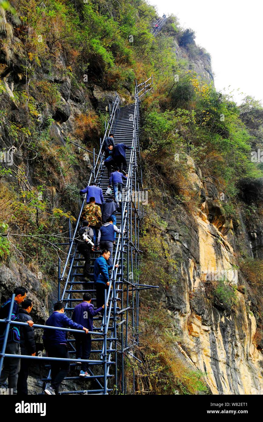 Tourists climb up an 800-meter cliff on a steel ladder in a mountainous ...