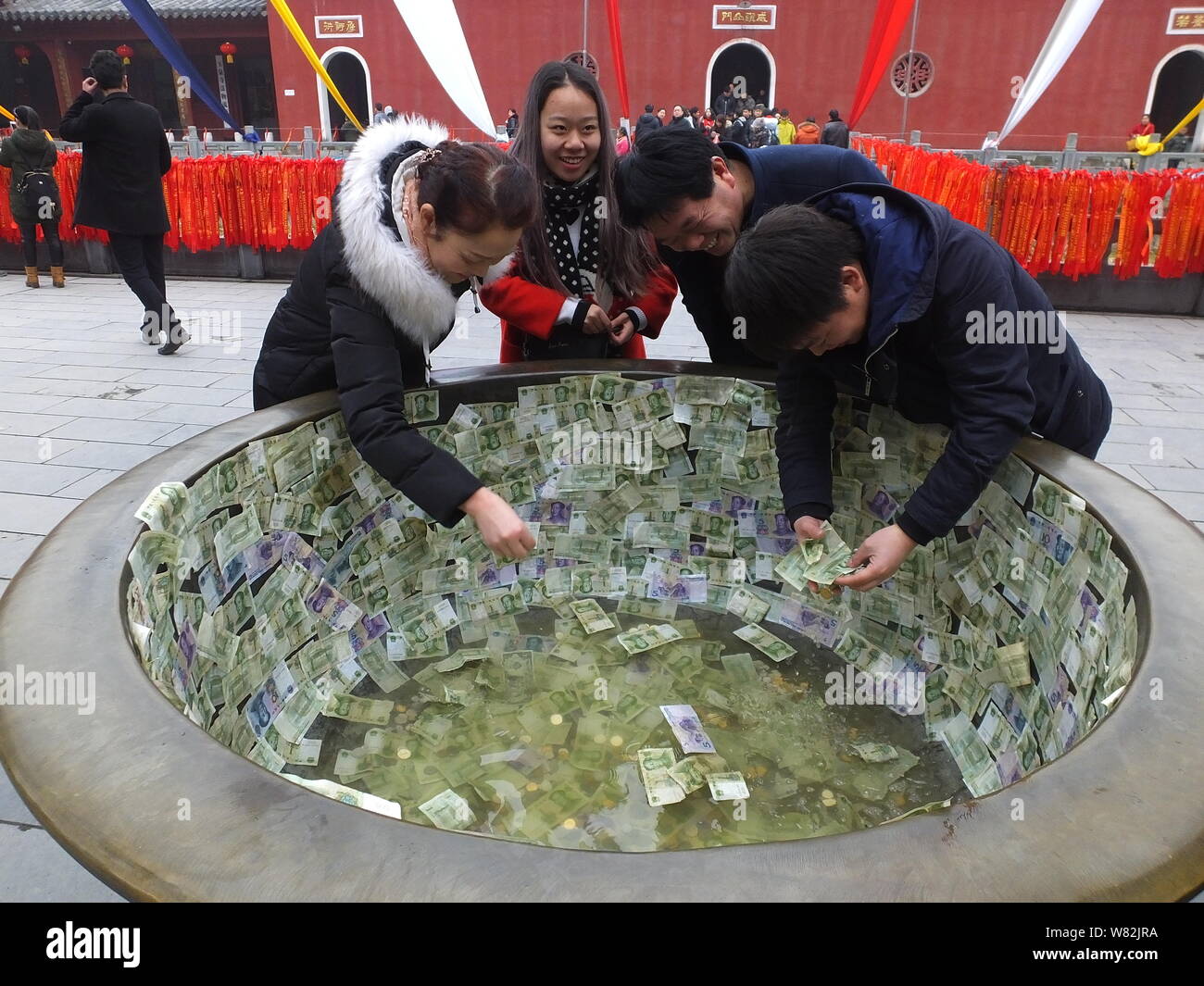 Chinese worshippers throw coins and banknotes into a vat to pray for ...