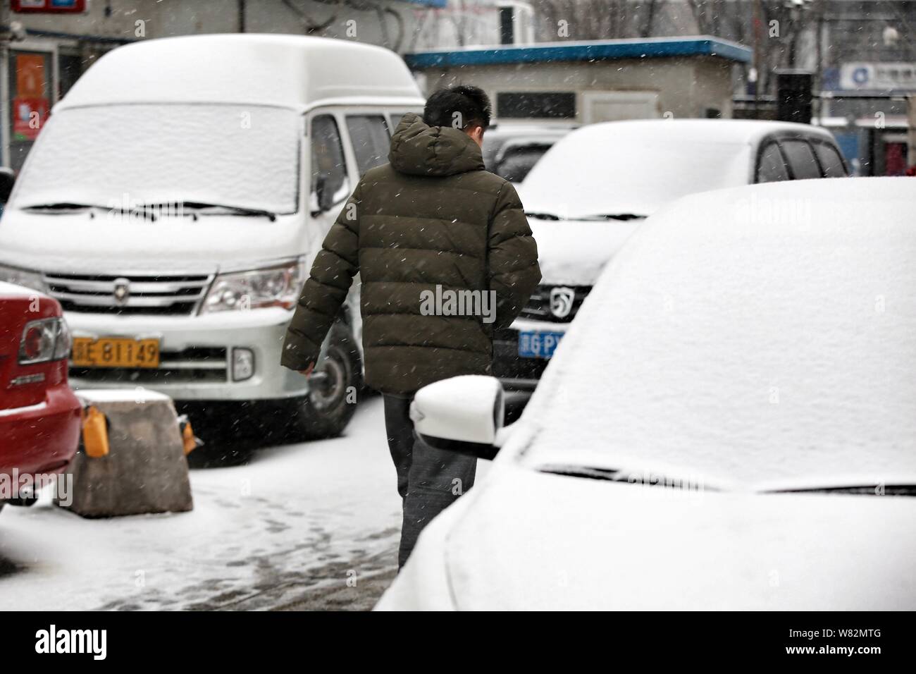 A pedestrian walks past snow-clad vehicles in heavy snow in Beijing ...