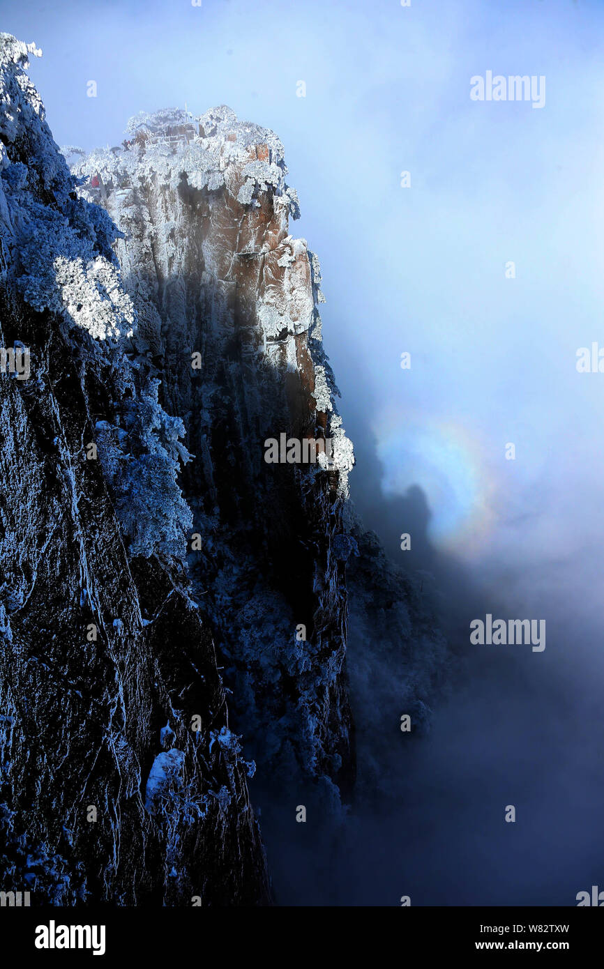 Landscape of pine trees covered with snow against a circular rainbow in the Huangshan Mountain ...