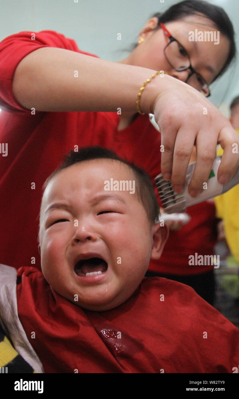 A young Chinese boy weeps while having his hair cut to celebrate the ...