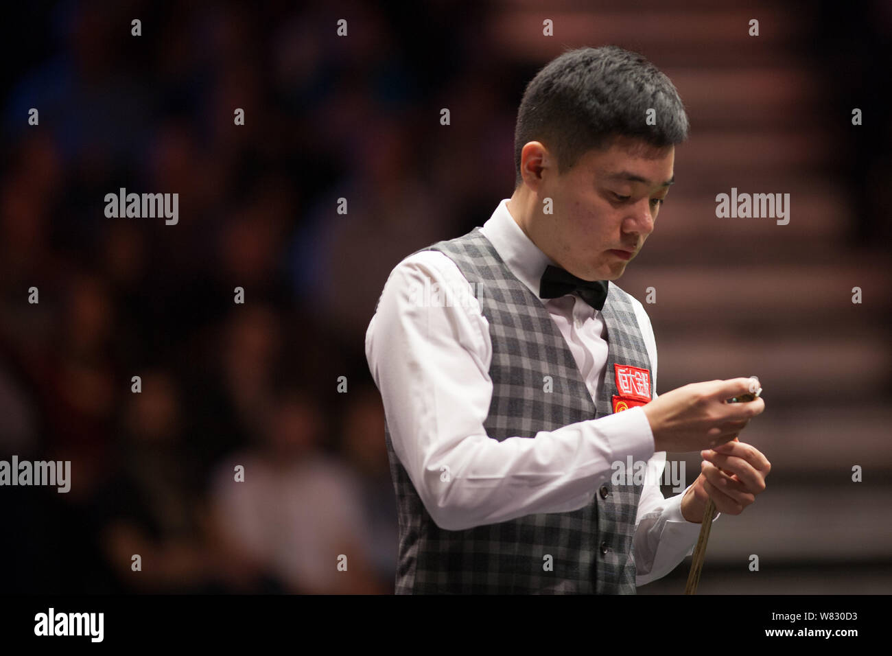 Ding Junhui of China chalks his cue as he considers a shot to Kyren Wilson of England in their ...