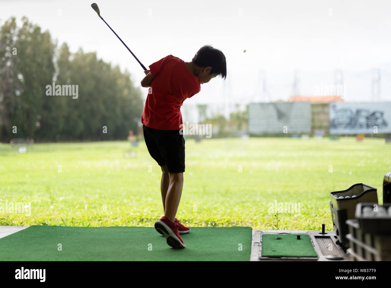 Young asian boy is practicing his golf swing at the golf driving range ...