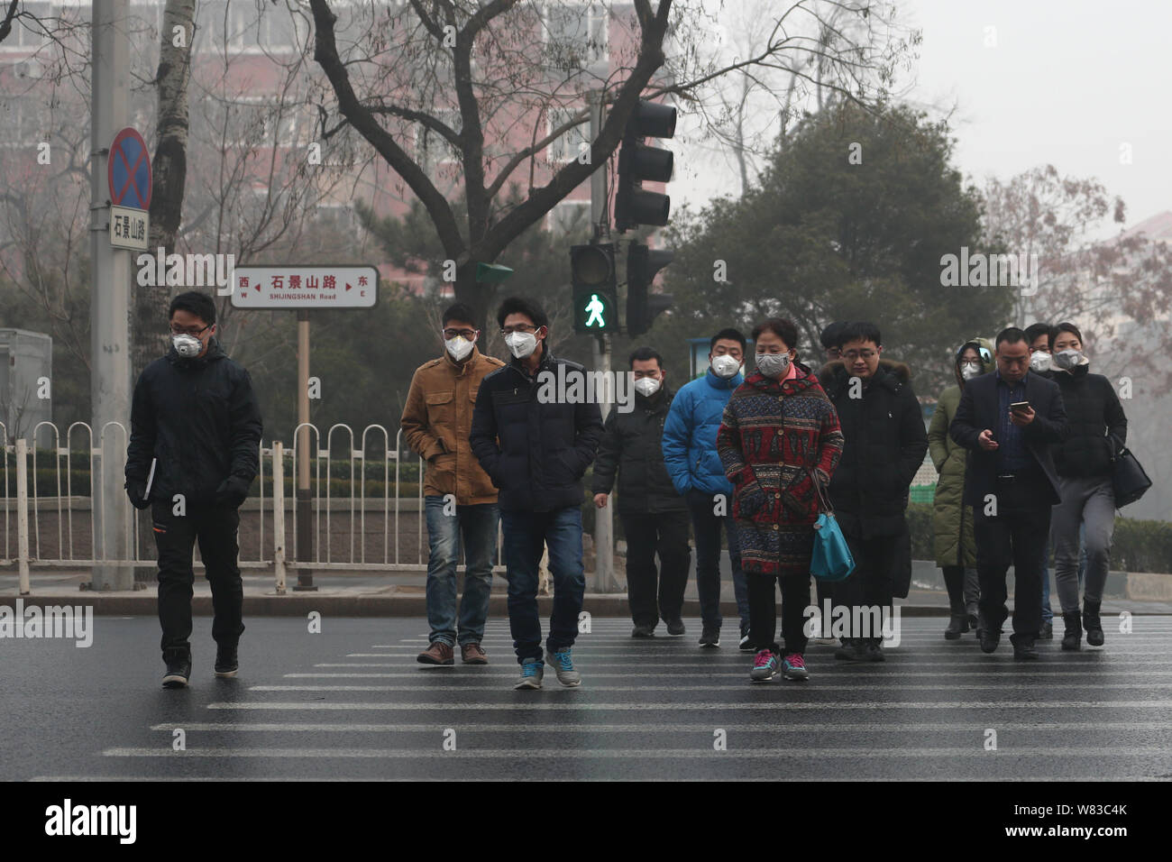 Pedestrians wearing face masks against air pollution walk across a road ...