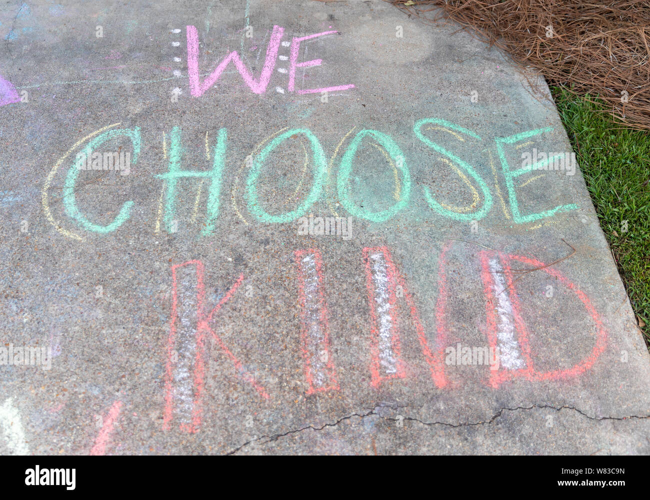 the words "We Choose Kind" written with sidewalk chalk on gray concrete ...