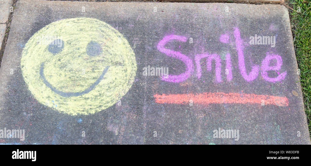 the word "Smile" amd a smiley face written with sidewalk chalk on gray ...