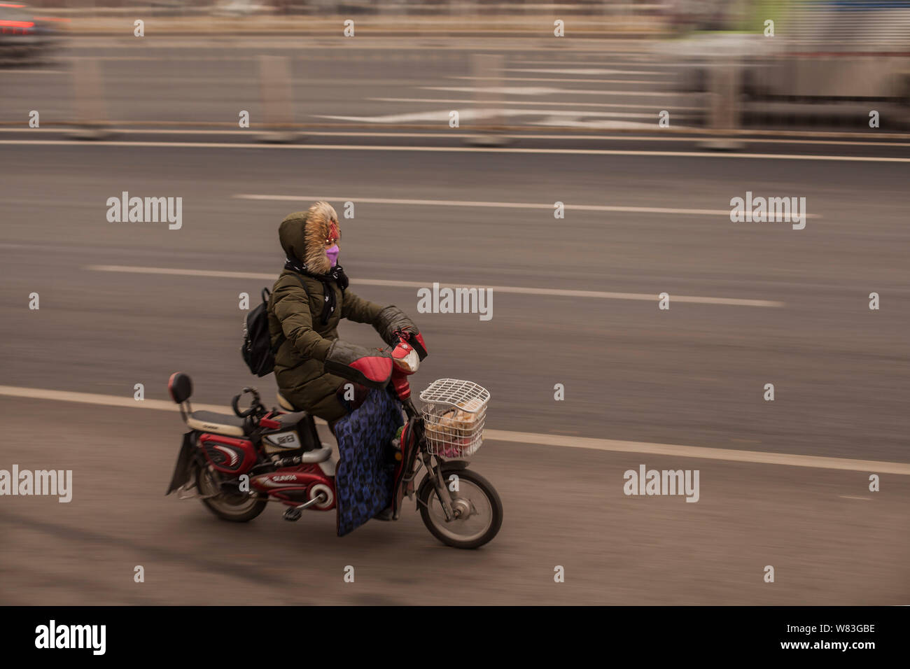A cyclist wearing a face mask against air pollution rides an electric ...