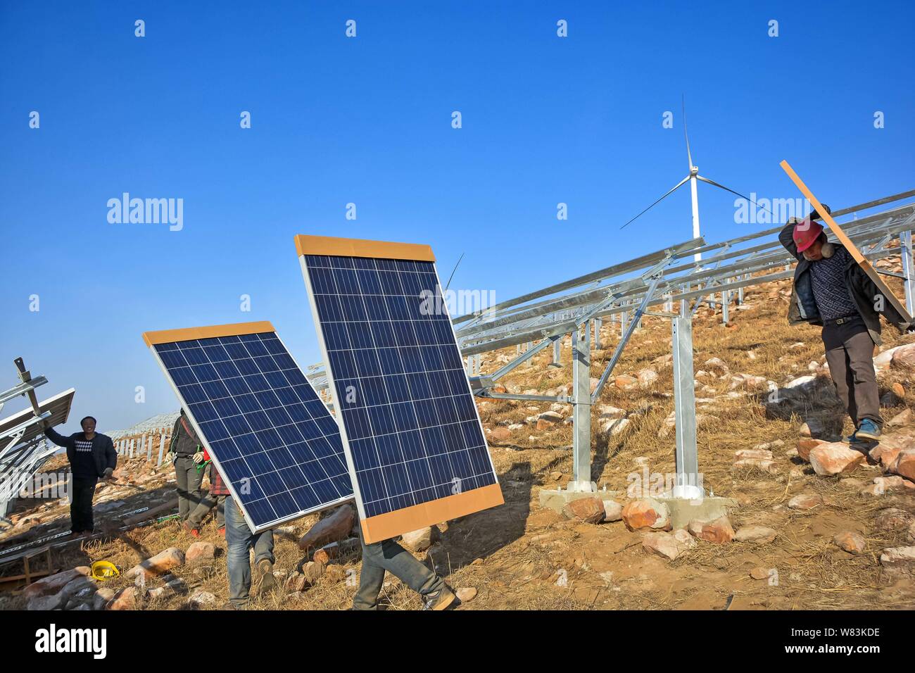 --FILE--Chinese workers install solar panels in front of wind turbines ...