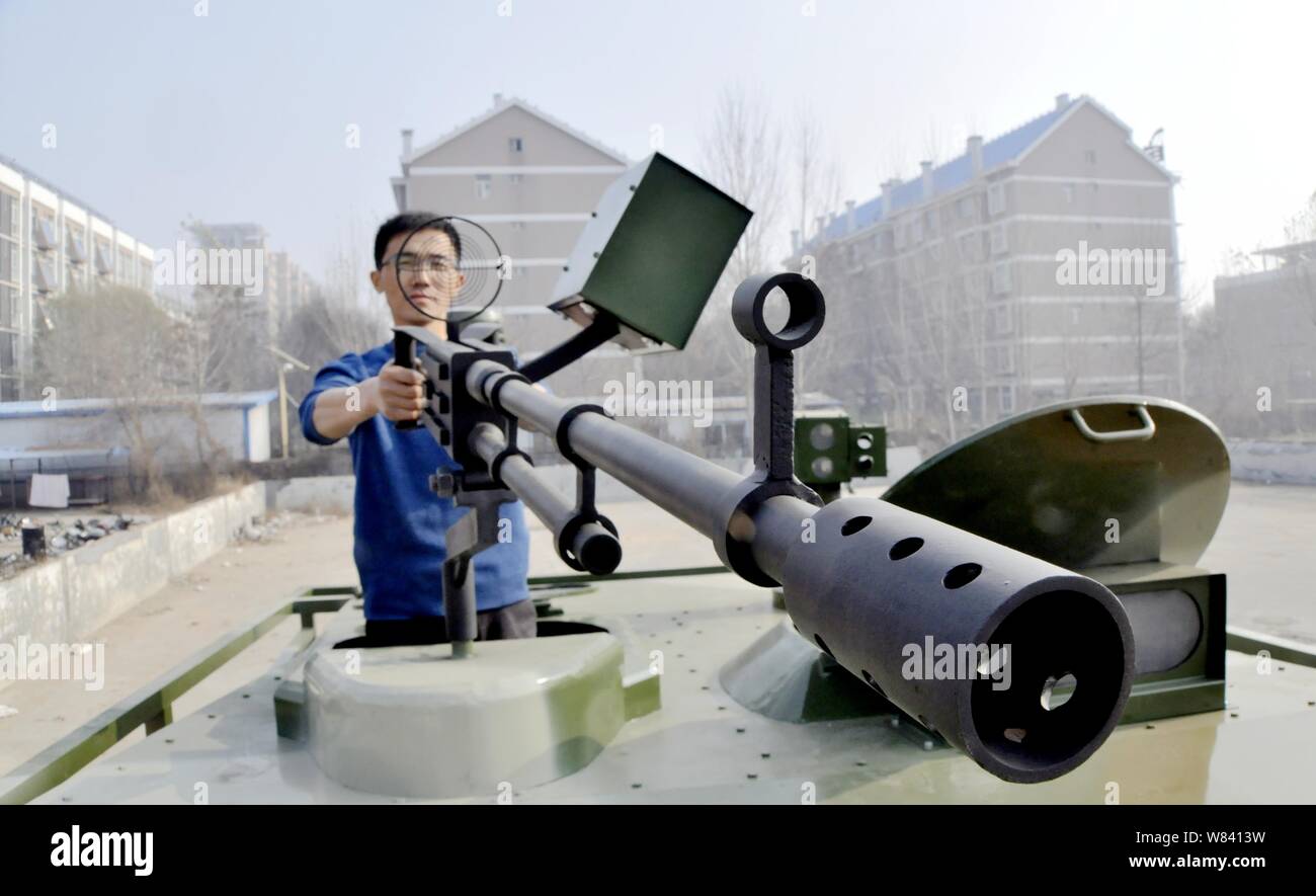 Chinese worker Xing Zhizhen holds a model machine gun on a replica of ...