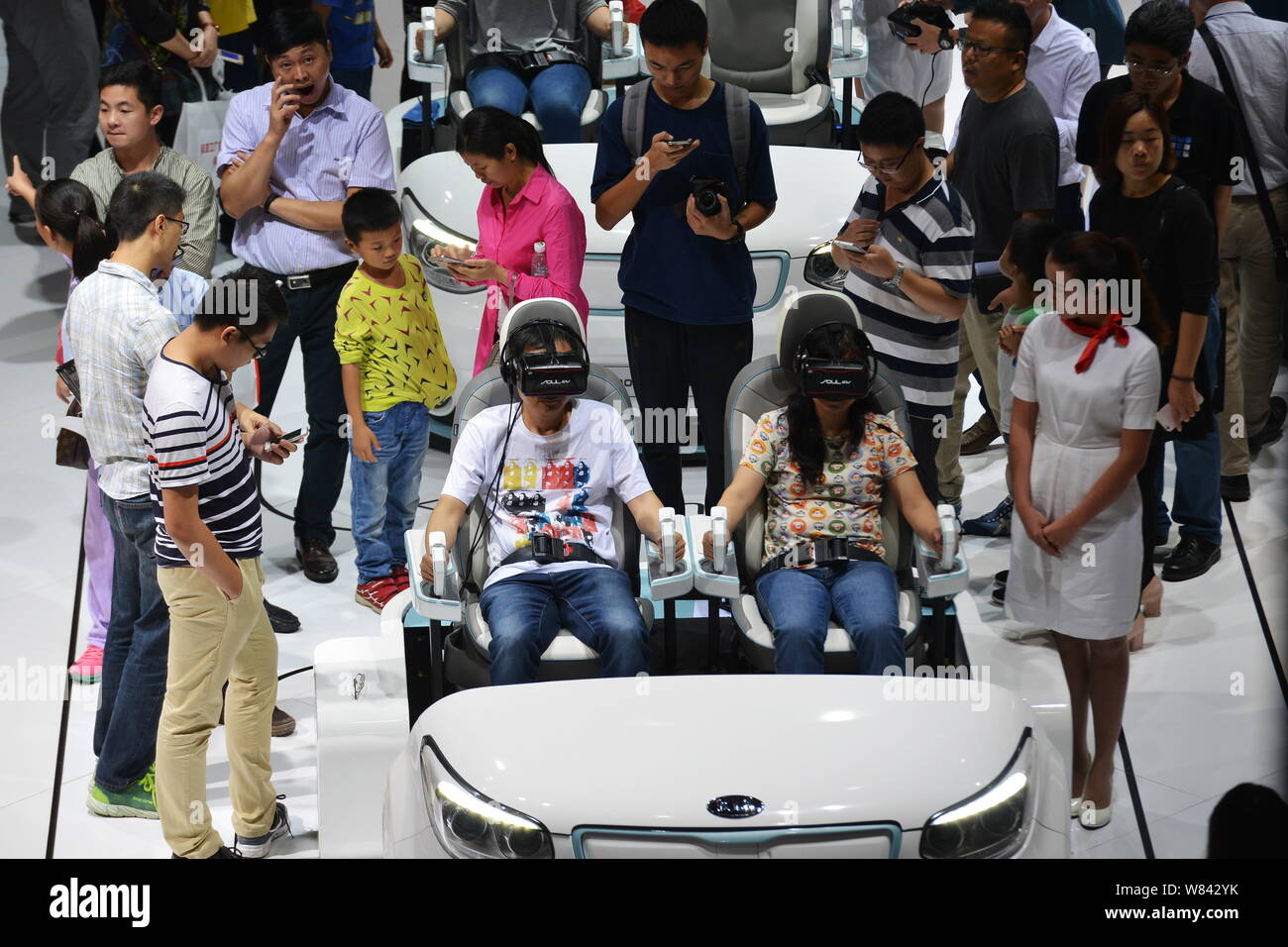Visitors wearing virtual reality (VR) devices sit in a model car to ...