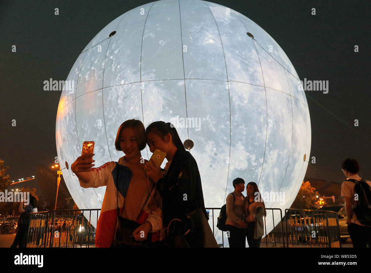 Visitors pose for selfies in front of a man-made moon with a diameter ...