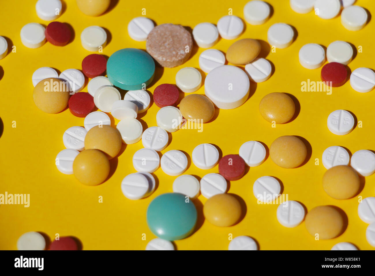 A lot of multi-colored pills on a yellow background. The tablets are ...