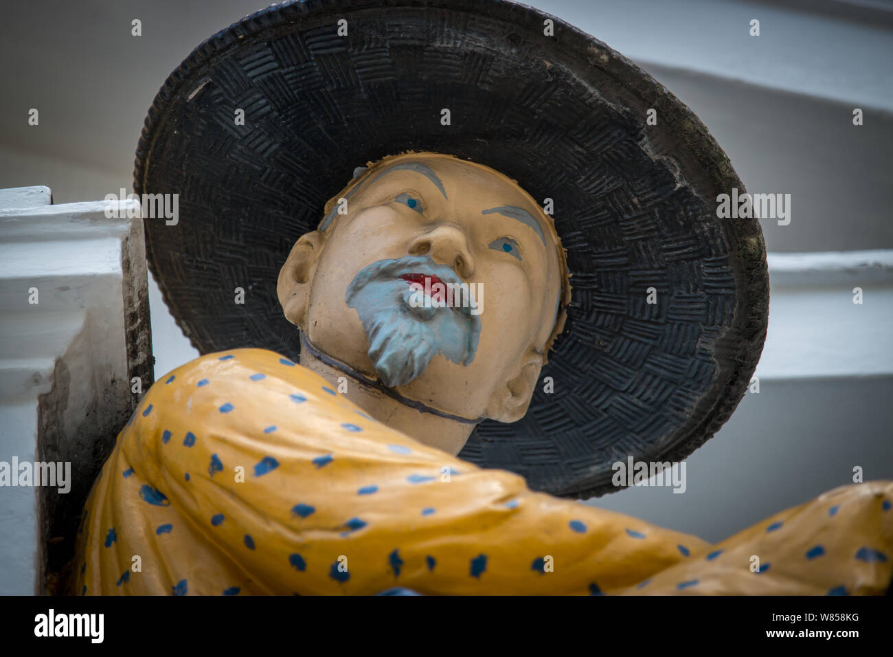 A close up of a carving of the face of a Chinaman wearing a hat over ...