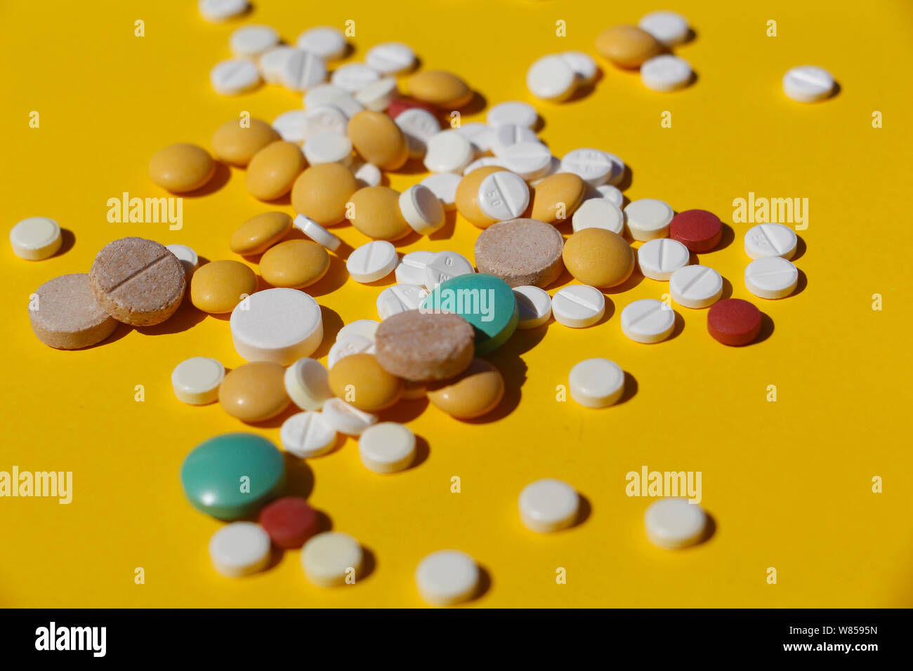 A lot of multi-colored pills on a yellow background. The tablets are ...