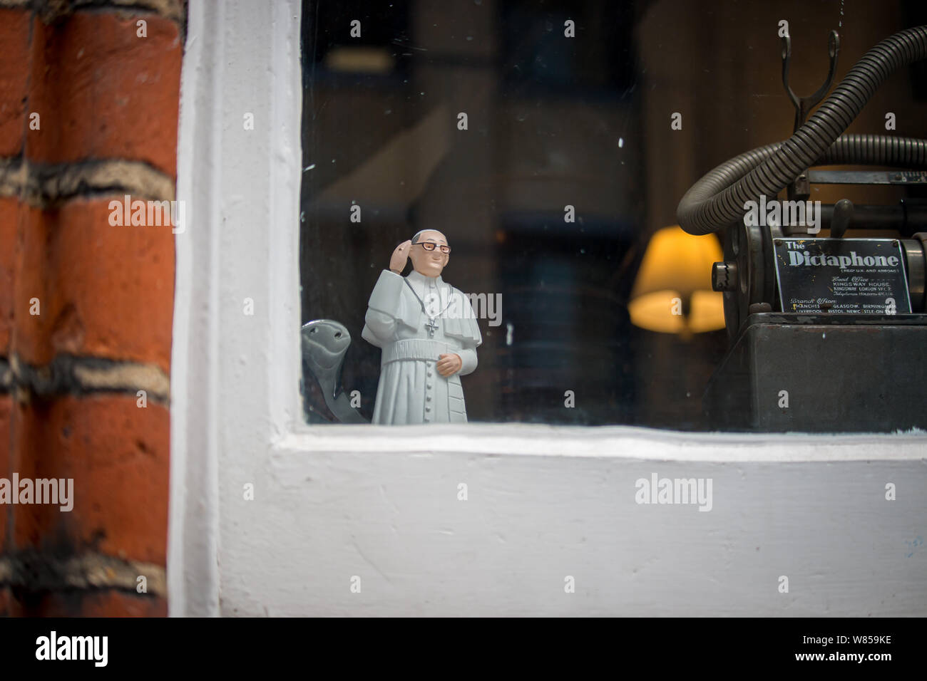 A pope figurine next to a Dictaphone in a window as seen from outside ...