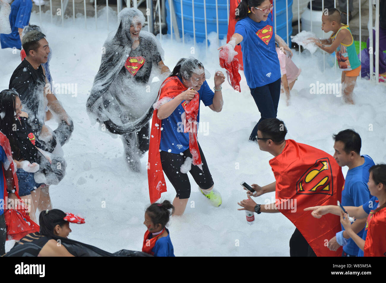 Participants dressed in costumes of Superman have fun with foam during ...