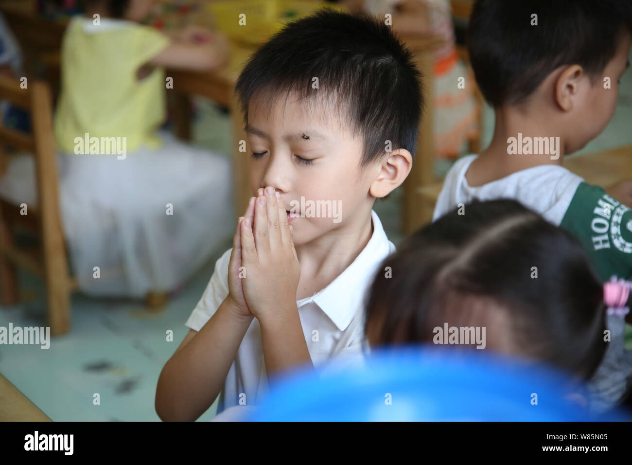 A young Chinese boy prays in the classroom at a kindergarten on the ...