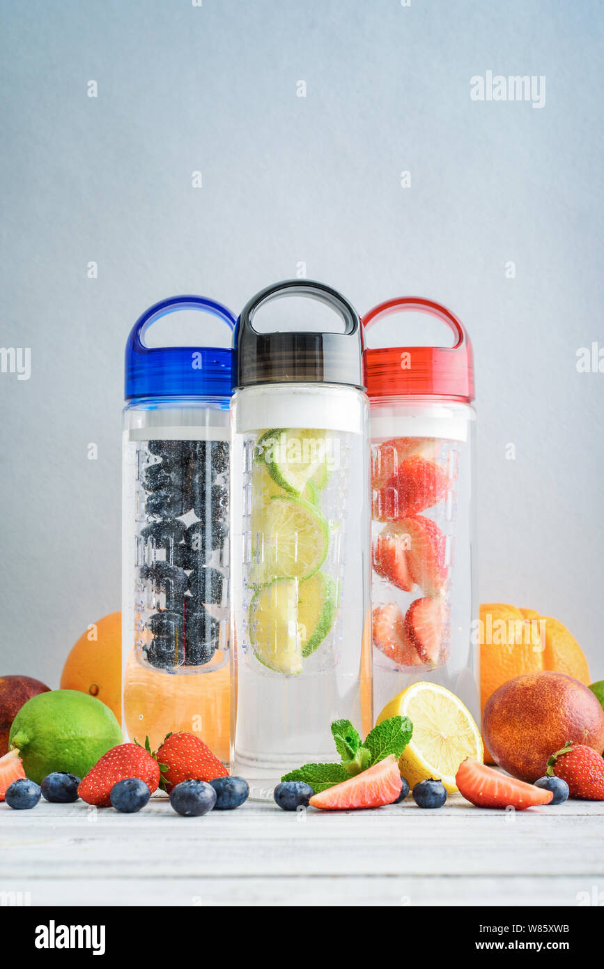 Infused detox water in bottles with fresh fruits and berries on light ...