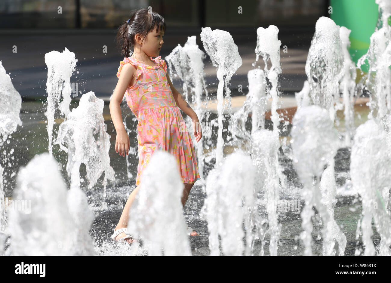 A young girl plays with water in a fountain to cool off on a scorcher ...