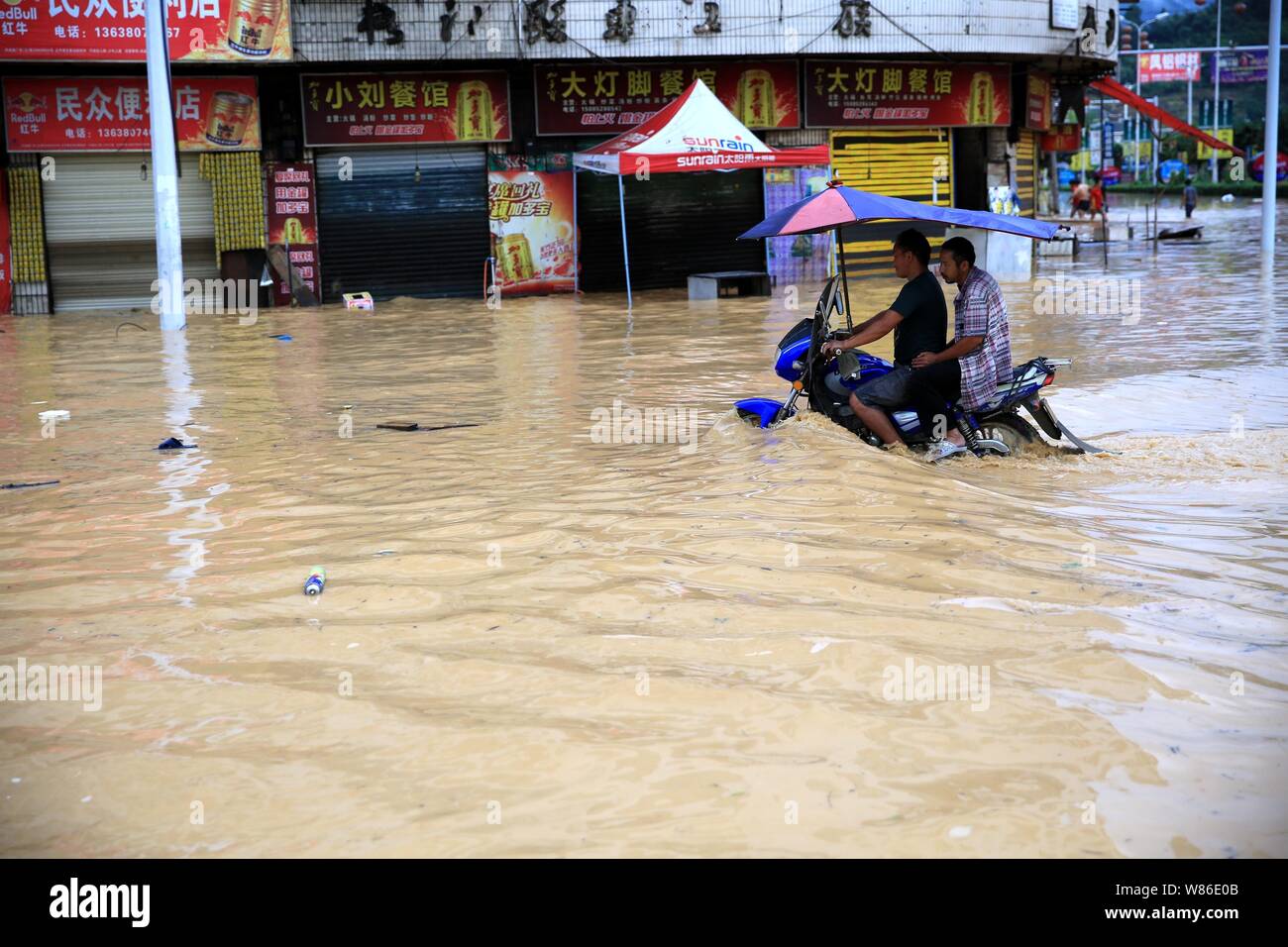 Chinese men ride a motorcycle on a flooded road caused by heavy rain in ...