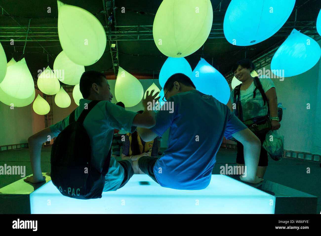 Visitors sit or stand under illuminated giant raindrop-shaped ...