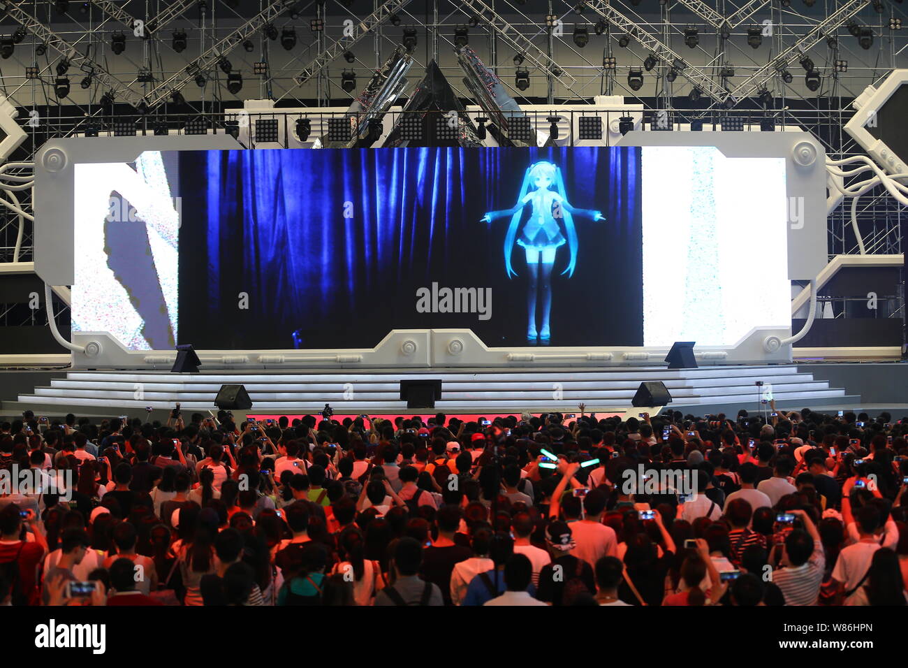 A crowd of visitors watch a performance of Hatsune Miku, a humanoid ...