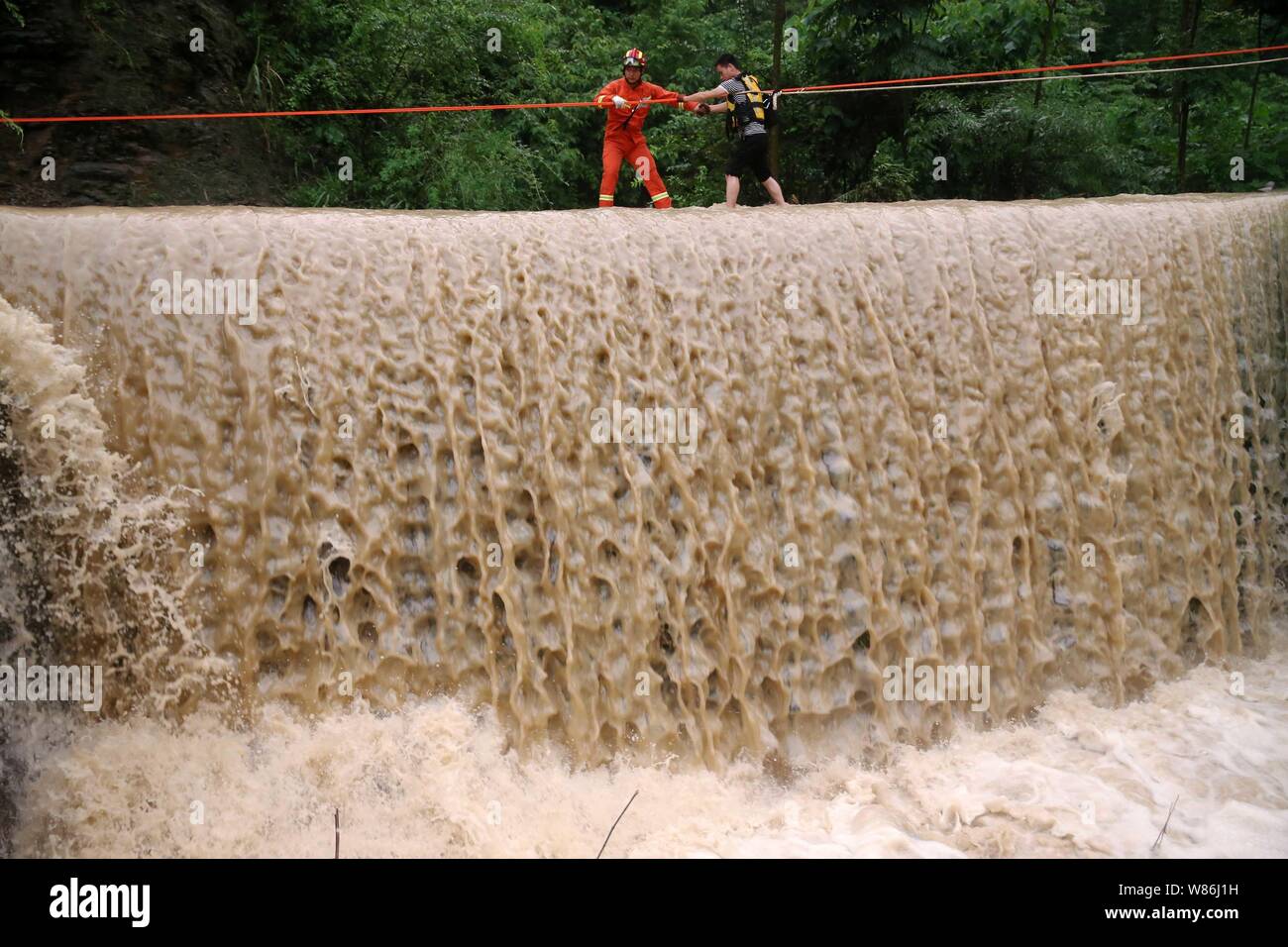 A firefighter assists a tourist to walk across floods caused by heavy ...