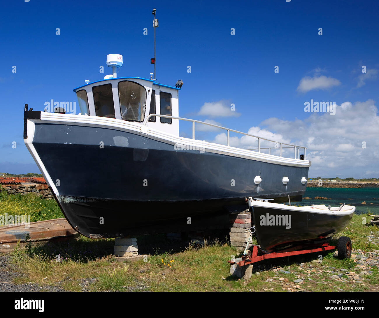 a small fishing boat raised on blocks on land with its tender boat on a ...