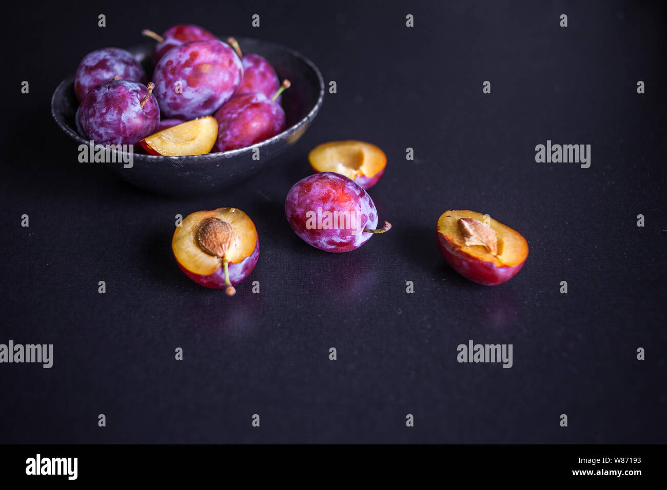 Fresh delicious plums in a plate on a black background. Summer fruits ...