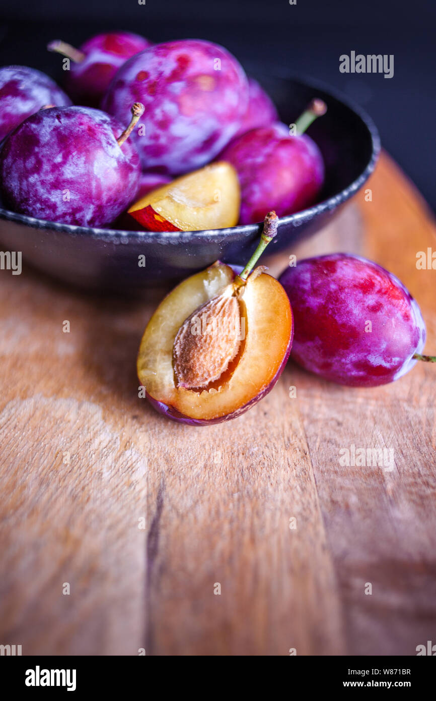 Delicious juicy blue plums in a plate on the table, textured wooden ...