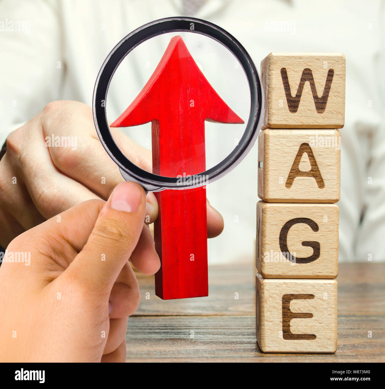 Businessman's hand holds red arrow up near wooden blocks with word Wage. Salary increase concept ...