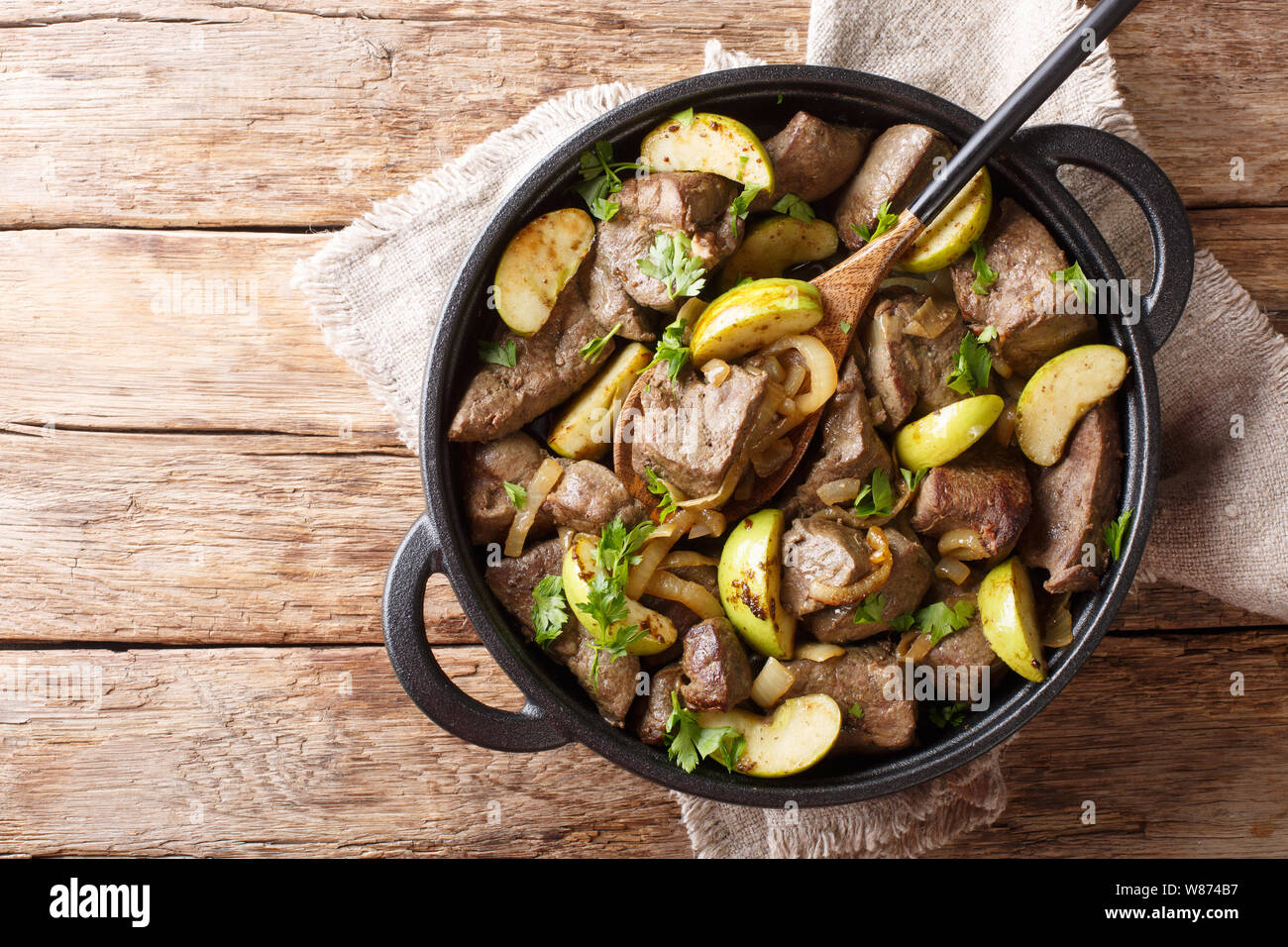 German food fried beef liver with green apples and onions close-up in a ...