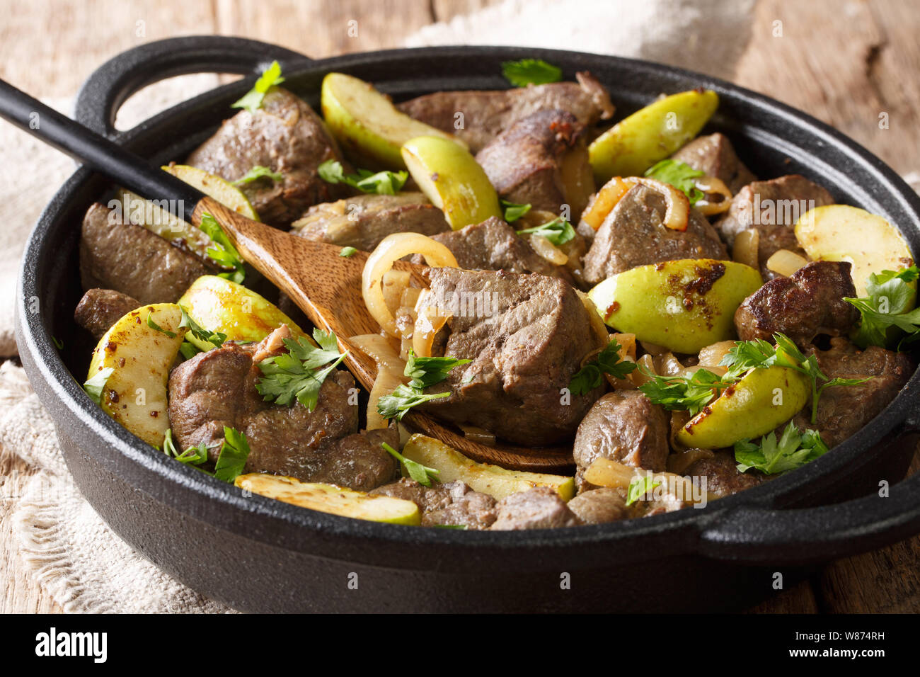 German food fried beef liver with green apples and onions close-up in a ...