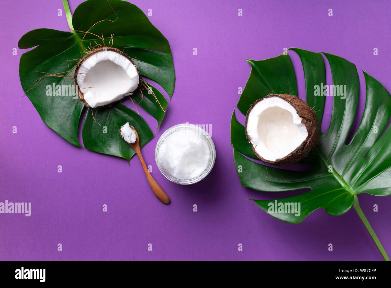 Coconut oil and ripe coconuts, tropical palm and monstera leaves on ...