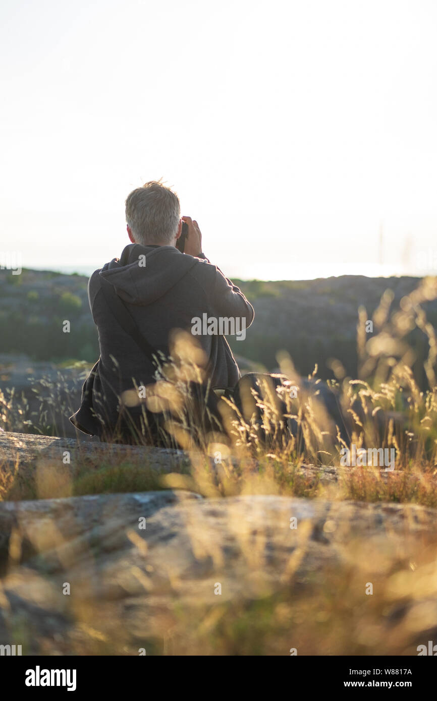 One man sitting on the rock taking a photo Stock Photo - Alamy