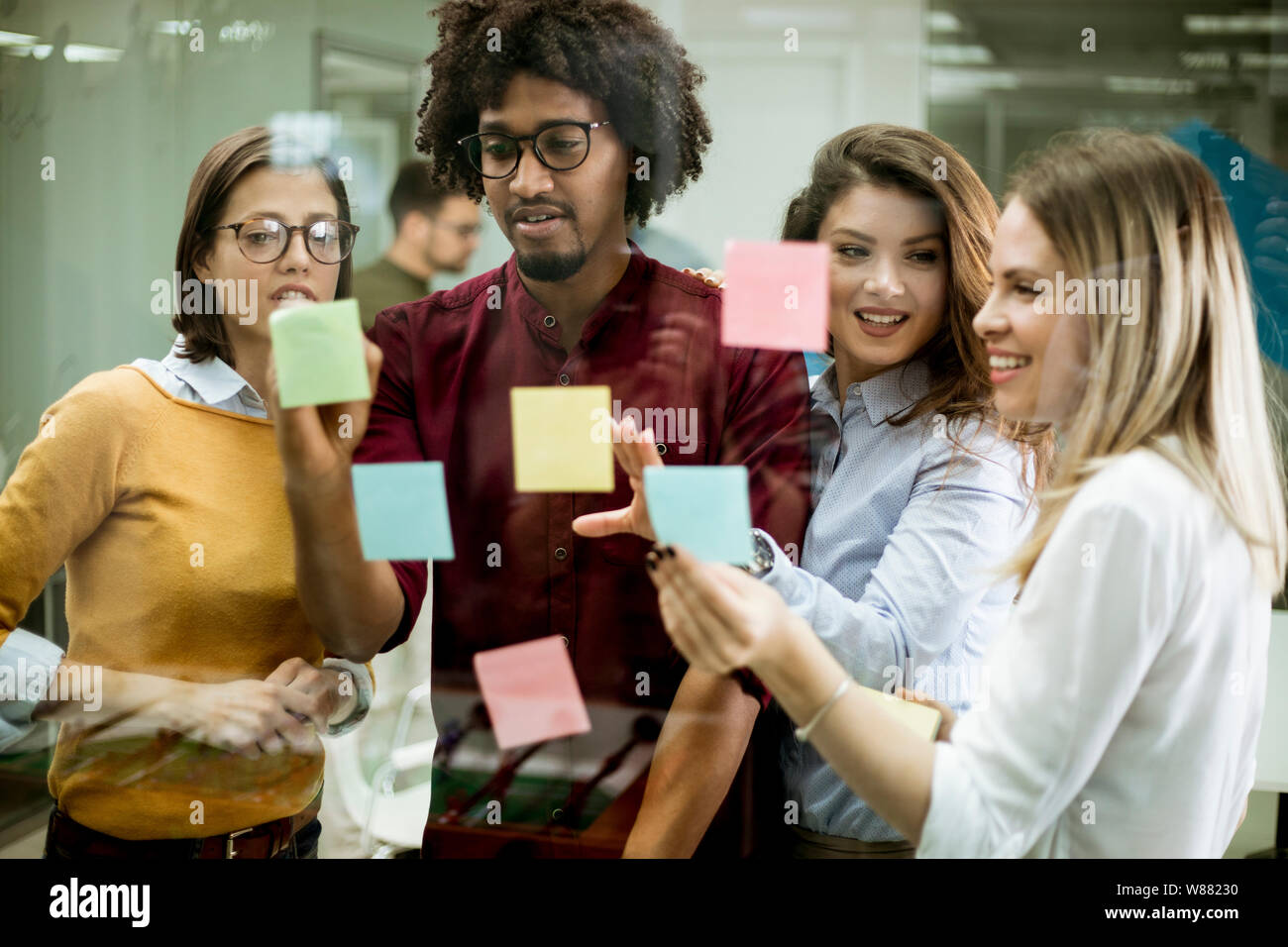 Group of young business people discussing in front of glass wall using ...