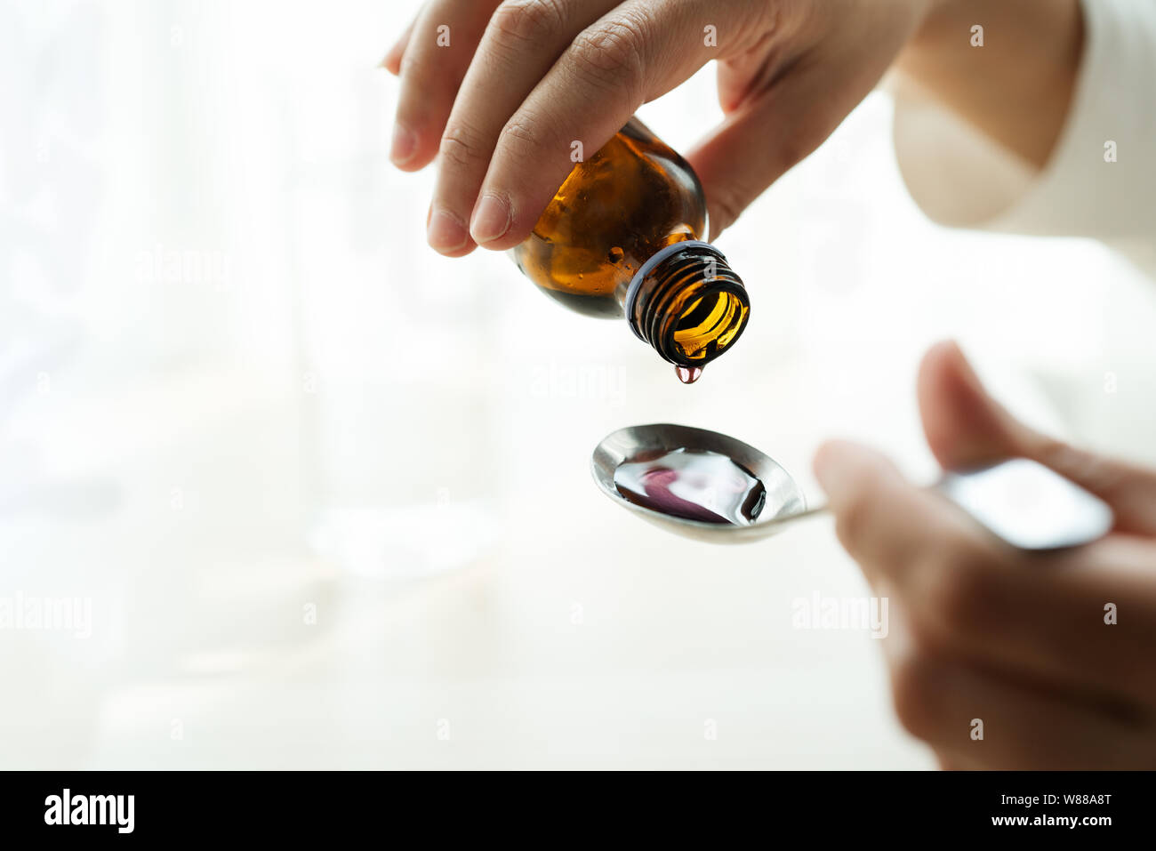 Woman hand pouring medication or cough syrup from bottle to spoon ...