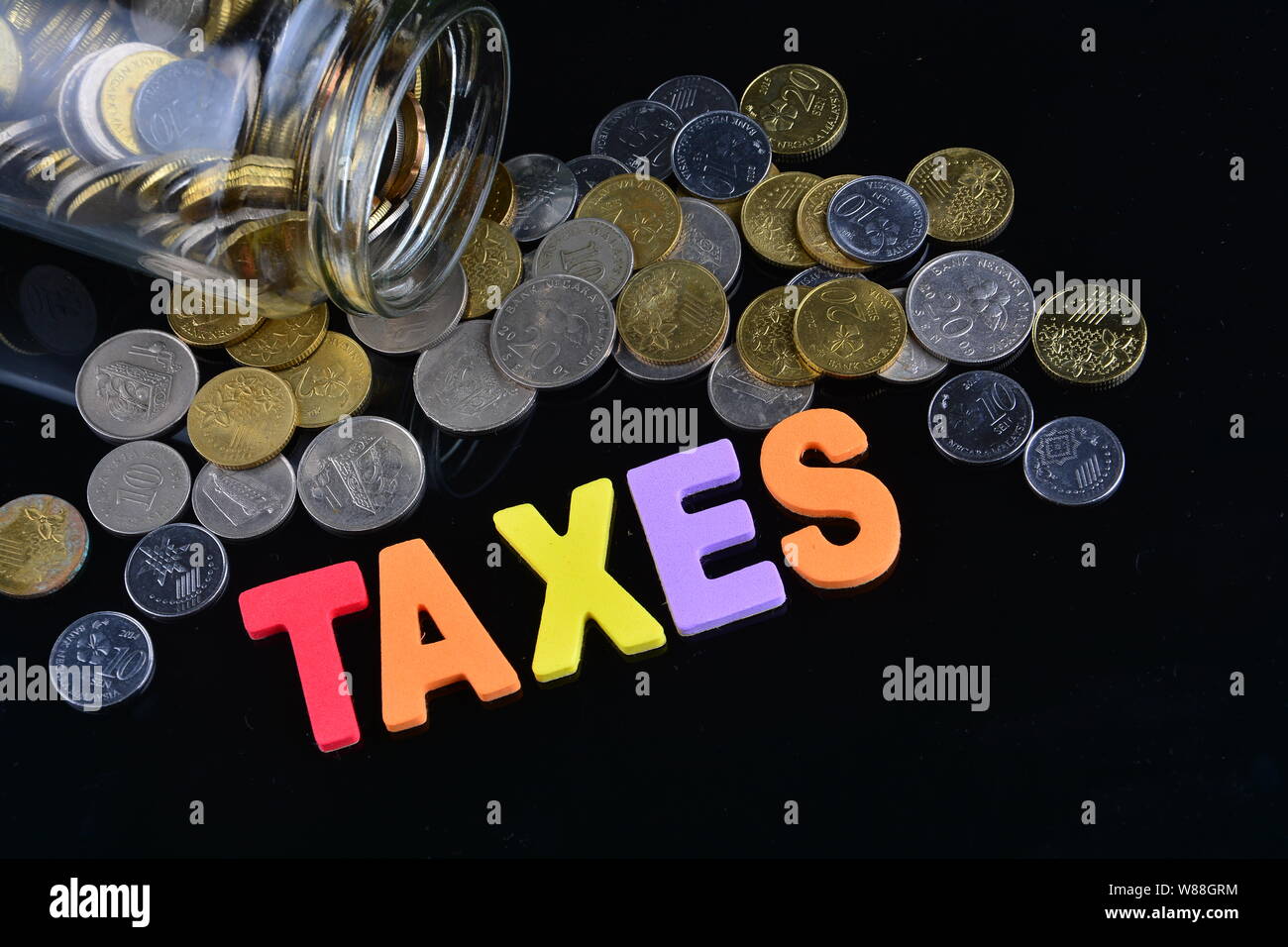 Coins spilling from a money jar with word TAXES Stock Photo - Alamy