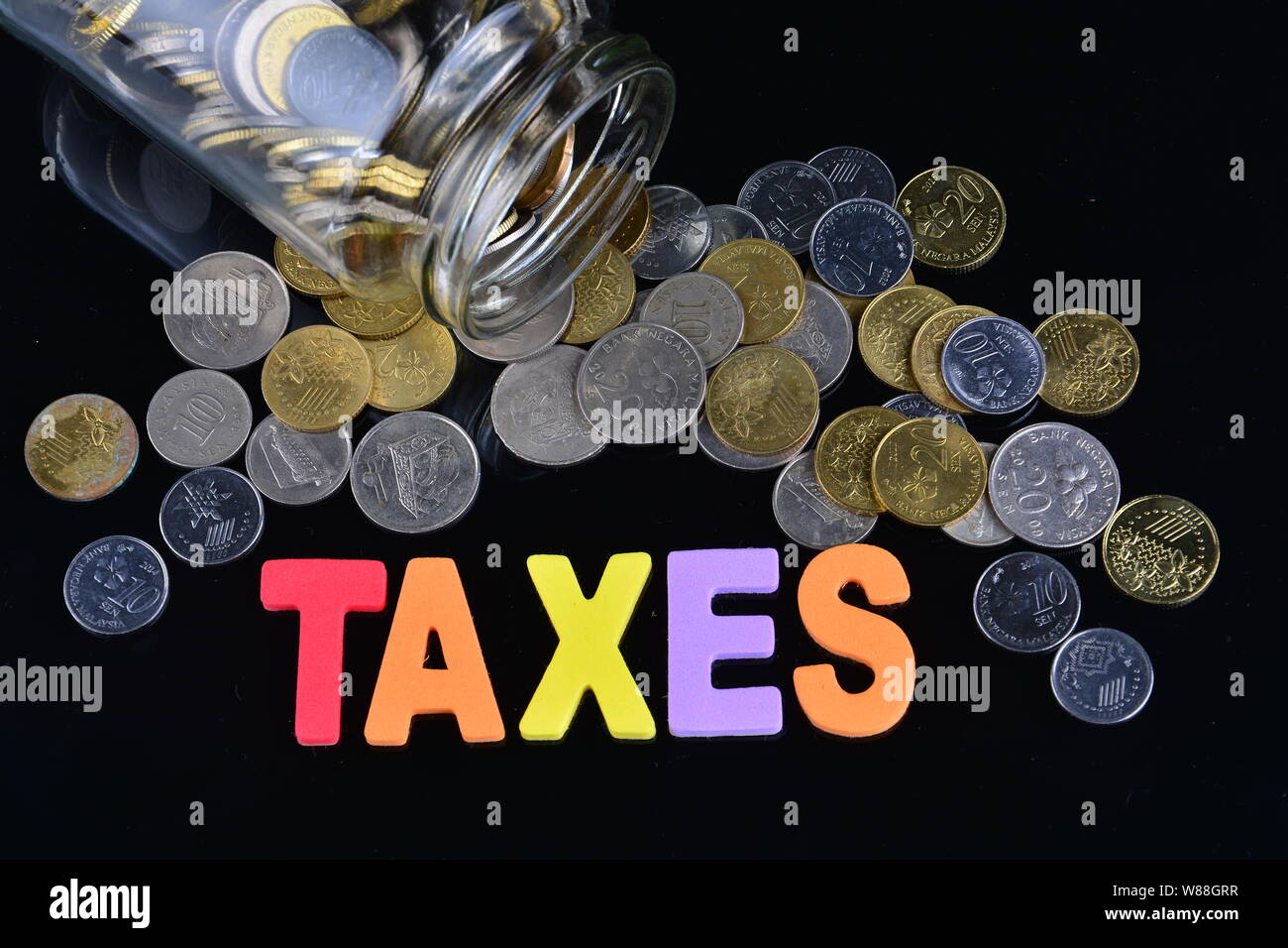 Coins spilling from a money jar with word TAXES Stock Photo - Alamy